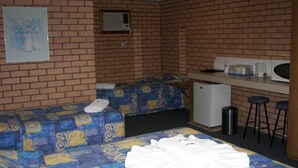 Quarto compacto com cozinha compacta, pequena geladeira, micro-ondas e um banquinho.
