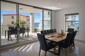 Uma área de jantar moderna com uma mesa grande, cadeiras pretas e vista para o oceano.
