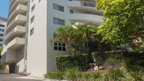 Um edifício moderno de vários andares com varandas e área ajardinada com árvores e arbustos.