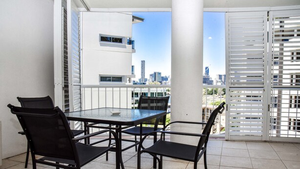 Uma varanda com mesa e cadeiras, corrimão branco e vista para a cidade.