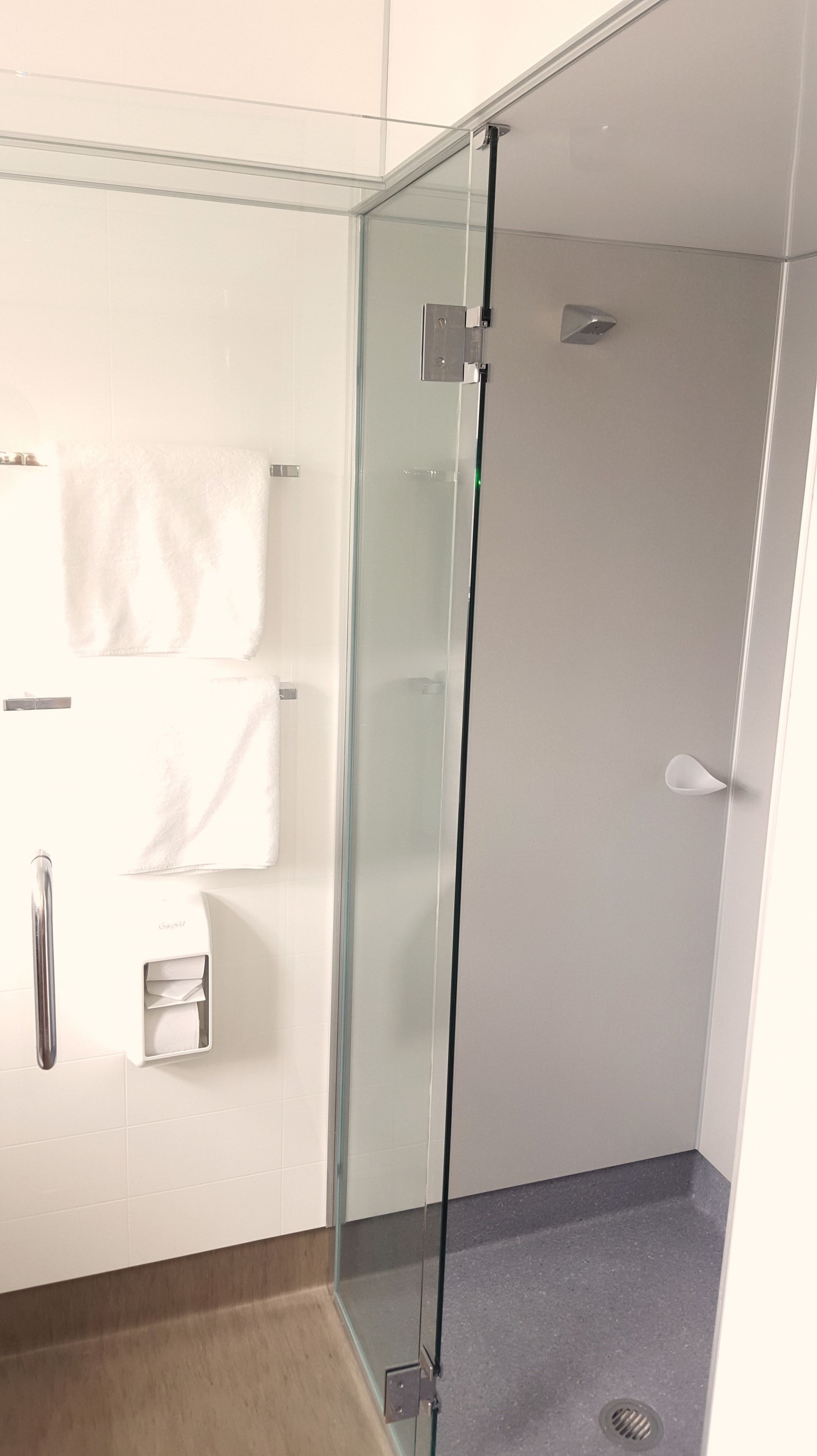 Uma casa de banho moderna com cabine de duche em vidro, um porta-toalhas com toalhas dobradas e um dispensador de papel higiénico.