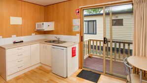 Cozinha compacta com micro-ondas, pia e uma pequena geladeira. Há uma porta de vidro corrediça que dá para um deck externo.