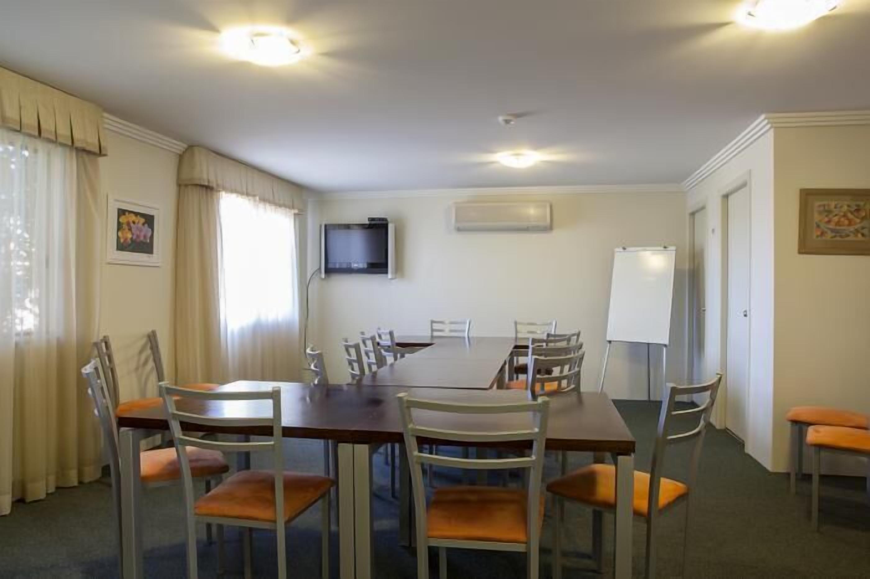 Uma sala de conferências com uma mesa comprida, cadeiras, um quadro branco e uma televisão na parede.
