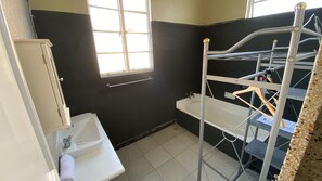 Casa de banho com uma pia branca, um espelho, uma janela e uma estante de metal.