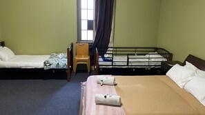 Quarto em dormitório com duas camas de solteiro, uma cadeira e uma janela com cortinas.