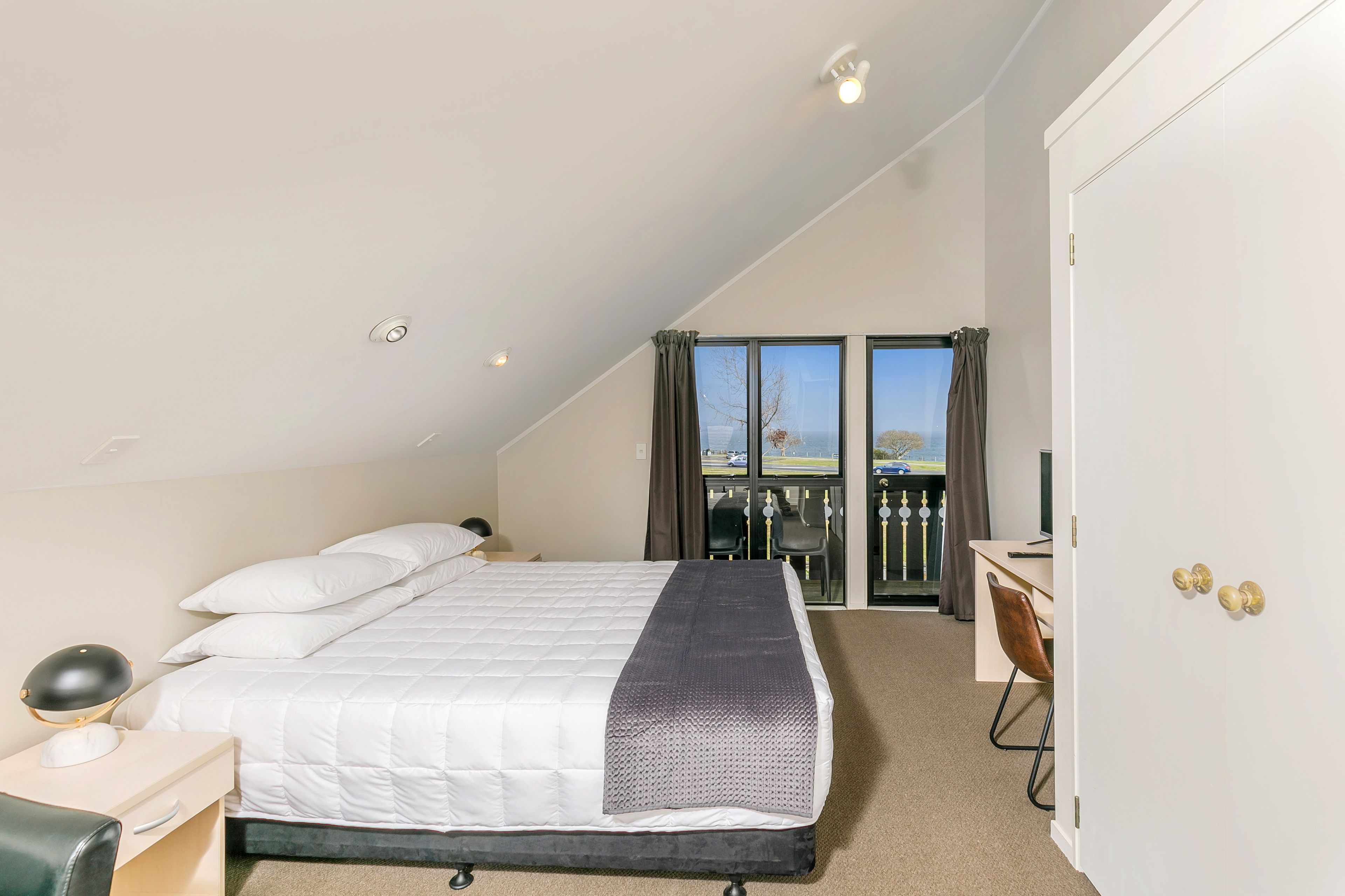 Quarto com cama, escrivaninha e vista para o exterior.