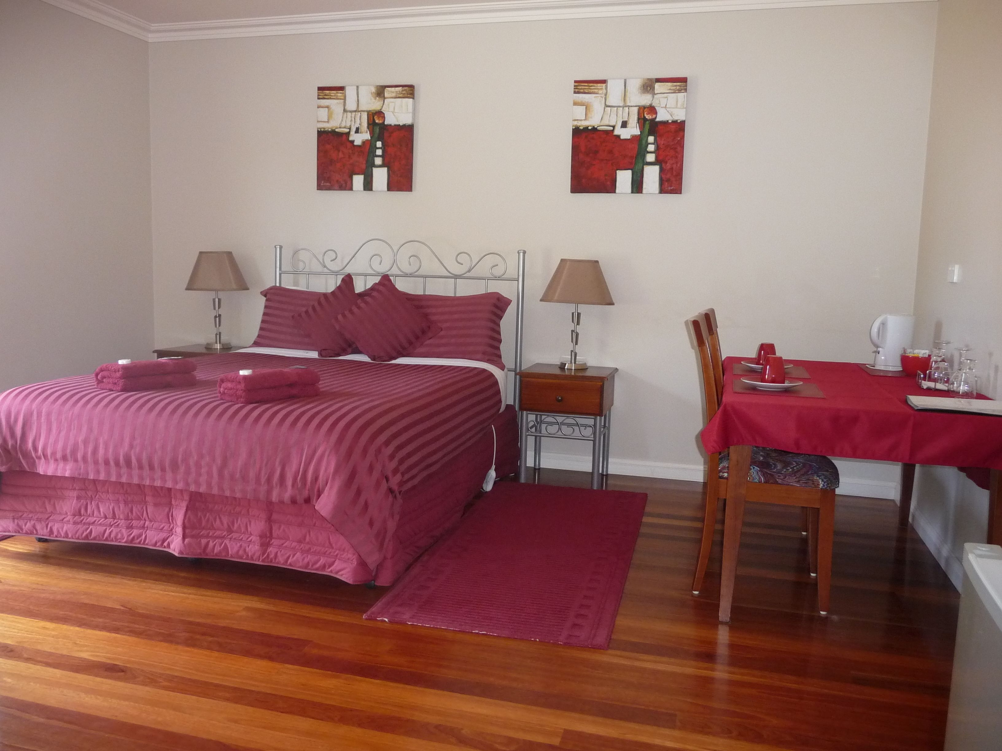 Um quarto com uma cama, duas mesas de cabeceira, uma cadeira, uma mesa e obras de arte nas paredes.