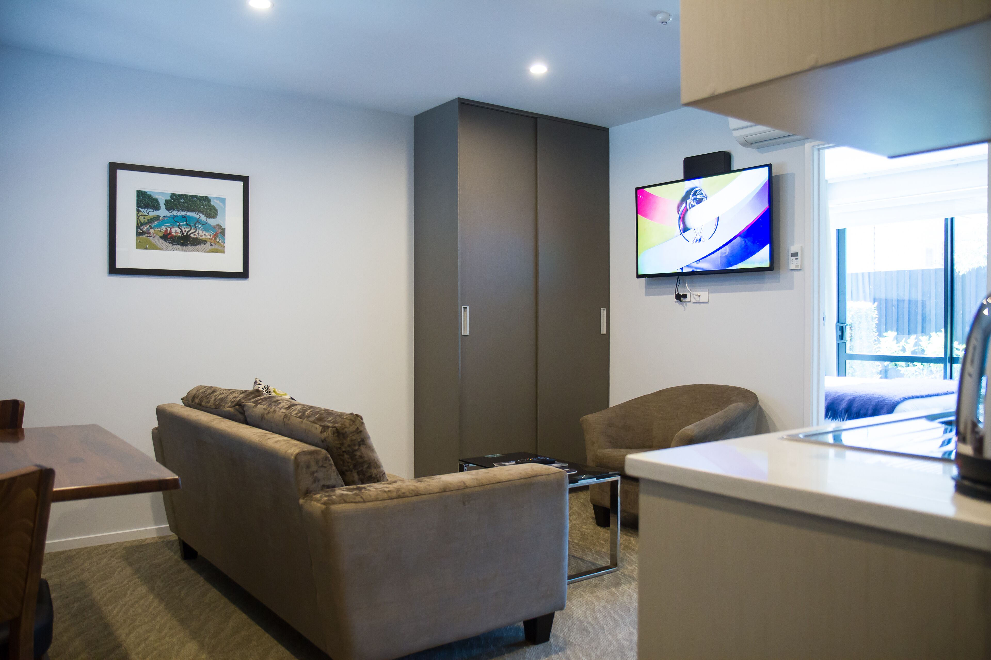 Uma sala de estar moderna com um sofá, uma mesinha, um armário e uma TV na parede.