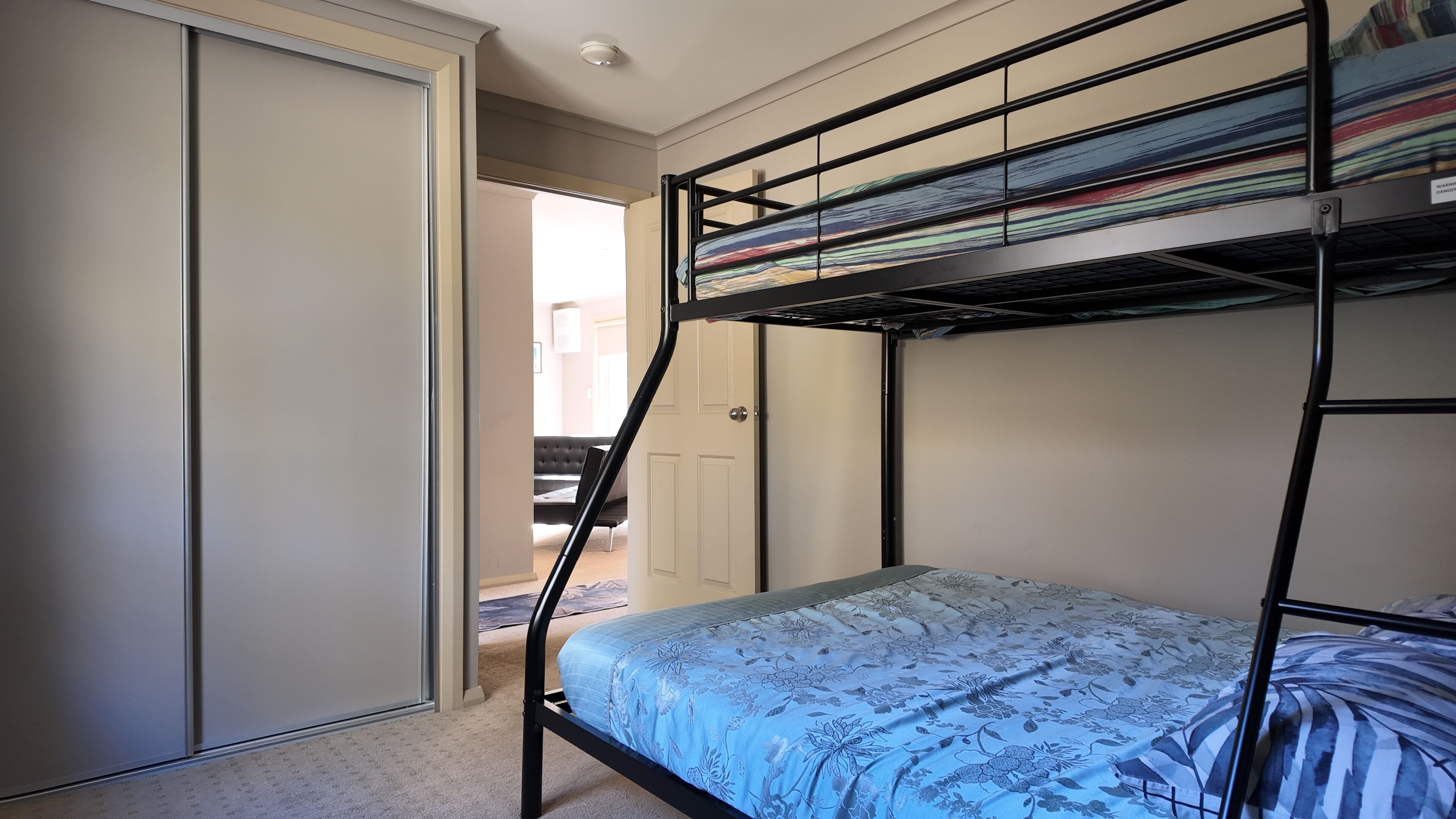 Uma cama beliche com colcha florida, uma porta fechada e um corredor que dá para outro quarto.