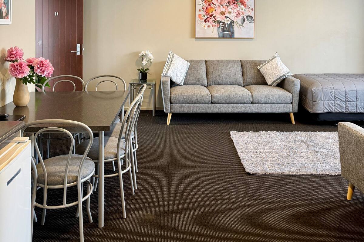 Uma sala de estar moderna com um sofá cinzento, uma mesa de jantar com cadeiras, um quadro na parede e uma porta com o número 11.