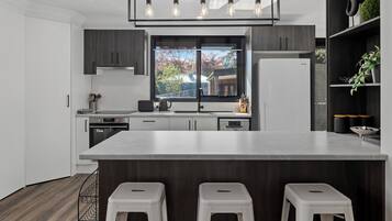 Cozinha moderna com armários de madeira escura, uma ilha grande com banquetas, uma janela com vista para árvores e um forno embutido.