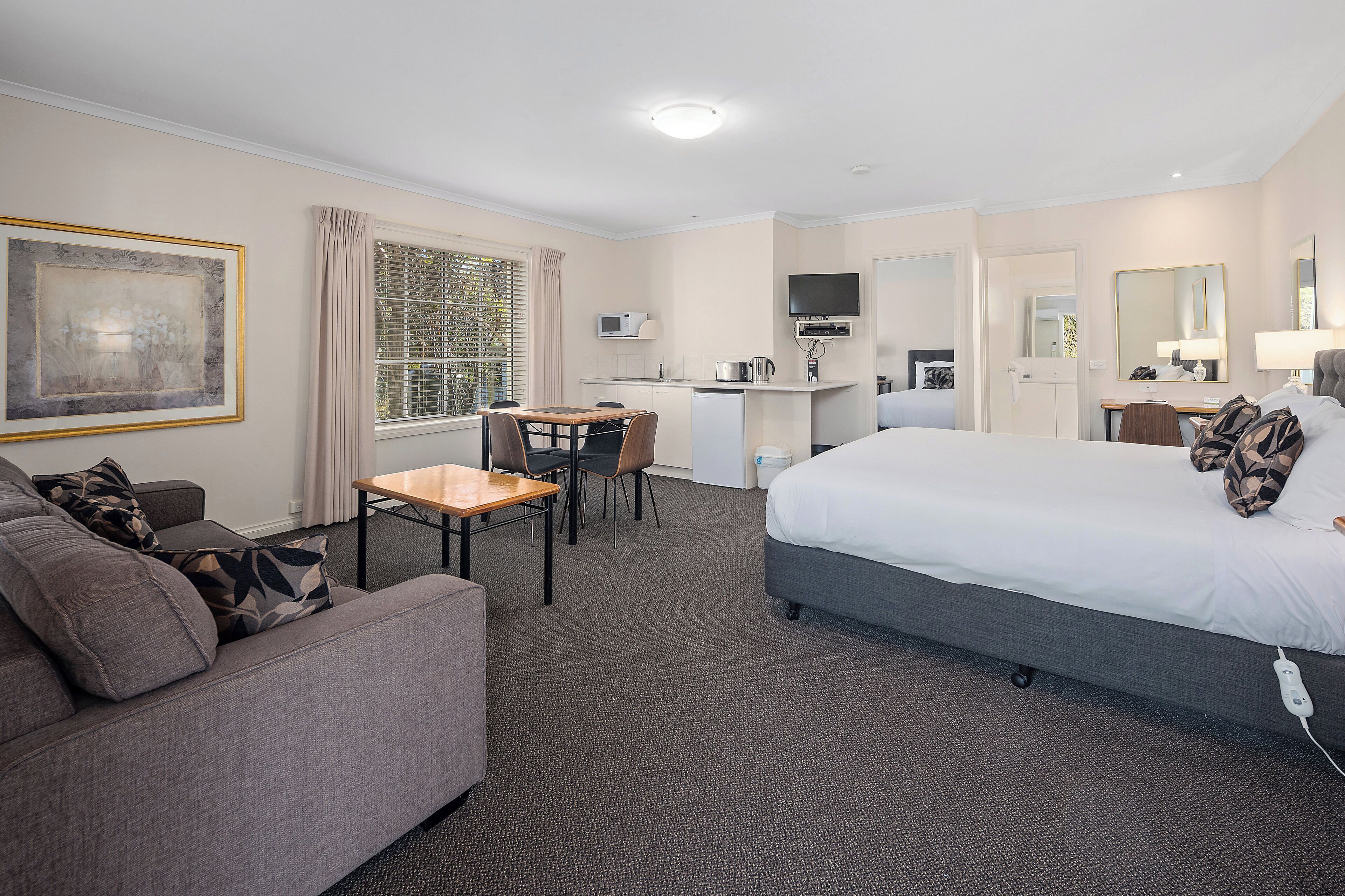 Quarto de hotel com cama, sofá, escrivaninha e televisão.