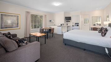 Quarto de hotel com cama, sofá, escrivaninha e televisão.