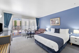 Quarto de hotel com uma cama grande, uma escrivaninha com computador, uma cadeira e uma varanda com vista.