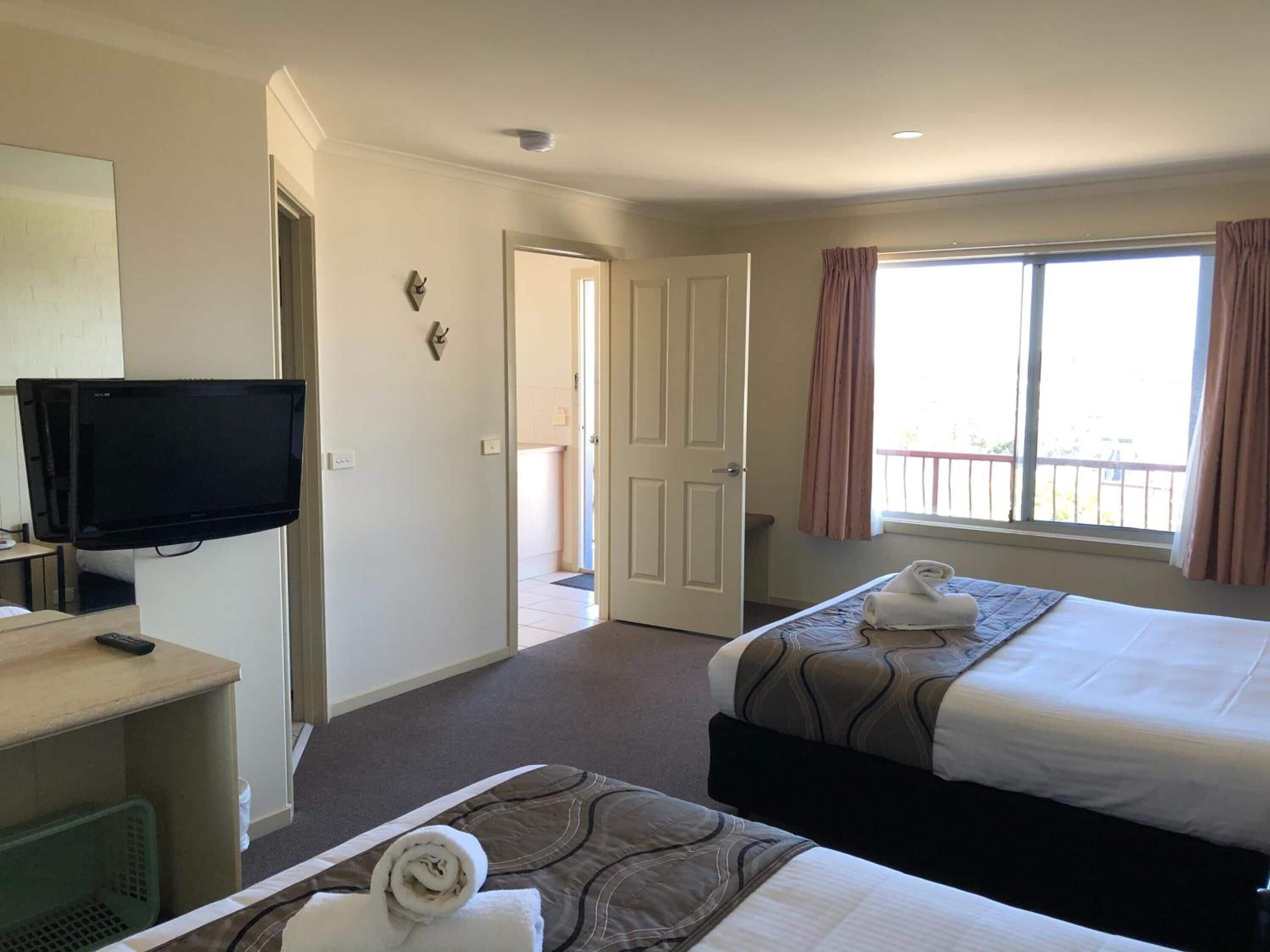 Quarto de hotel com cama, televisão, escrivaninha e janela com cortinas.