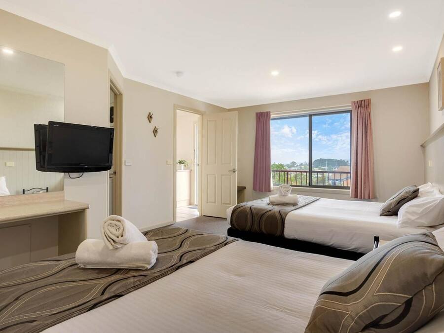 Quarto de hotel com duas camas, televisão, janela ampla com vista e varanda.