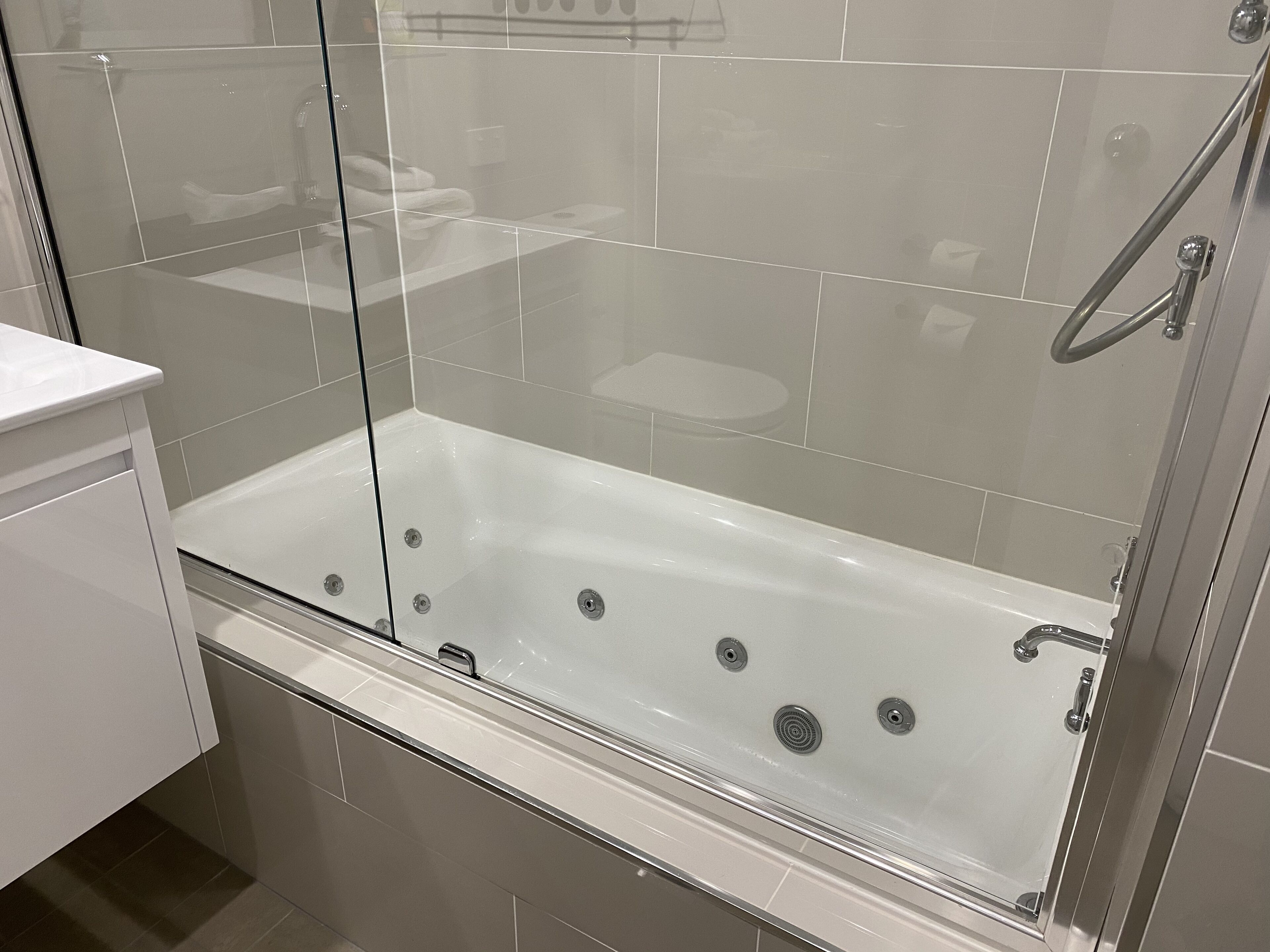 Uma casa de banho moderna com chuveiro de cabine de vidro, uma banheira branca e uma sanita pequena.