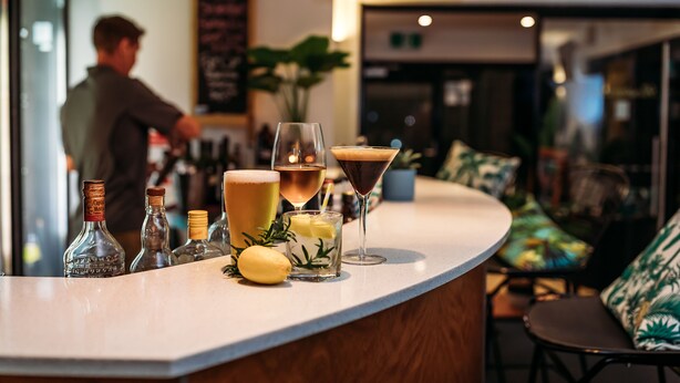 Balcão de bar com diversos copos e garrafas, um limão e um copo com bebida.