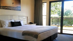 Uma cama grande com roupa de cama branca e cinza, um criado-mudo com um telefone, e um quadro de um moinho de vento na parede.