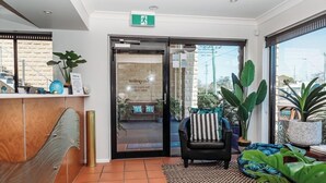 Uma área de recepção com porta de vidro, um sofá de couro preto e um tapete estampado.