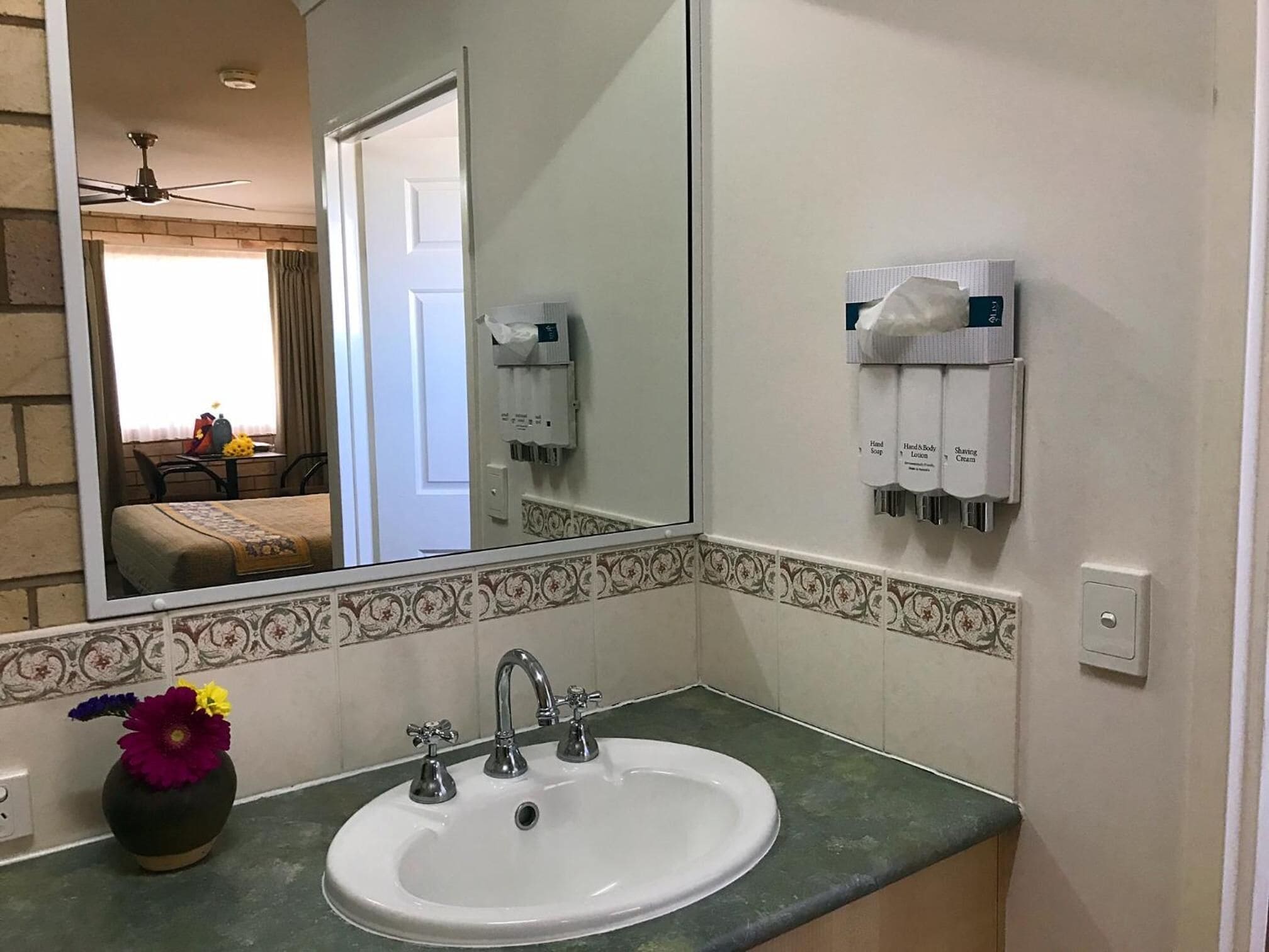 Casa de banho com lavatório branco, duas torneiras, espelho e dispensador de sabonete líquido.