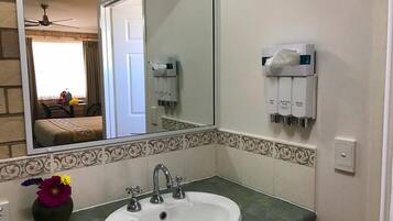 Casa de banho com lavatório branco, duas torneiras, espelho e dispensador de sabonete líquido.