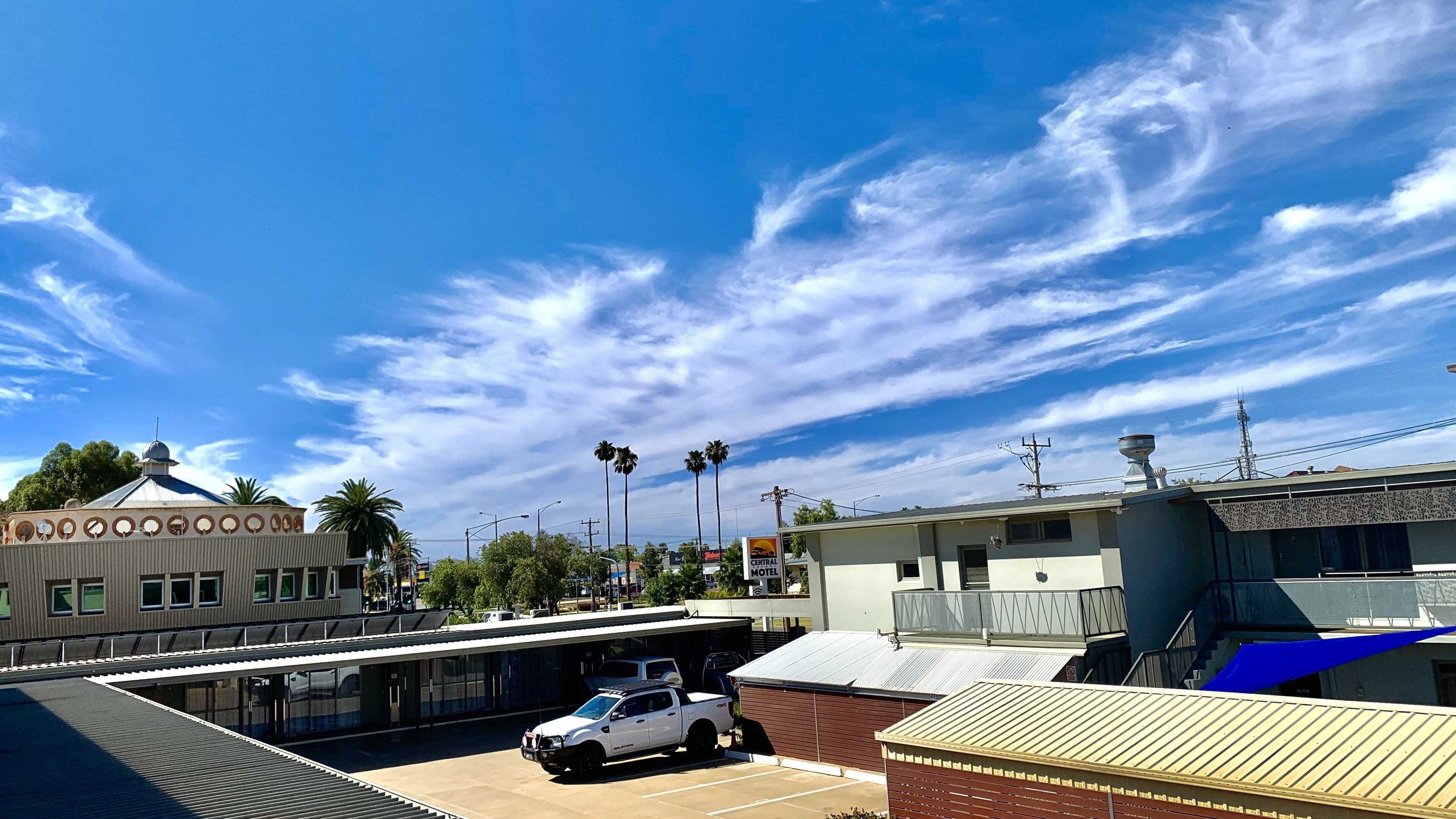 Um motel com área de estacionamento, um edifício com projeto de telhado característico e um céu azul claro com nuvens.