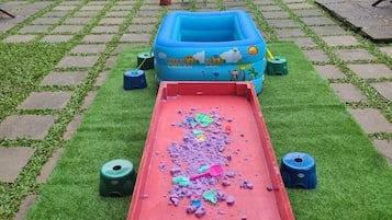 Um quintal com um caixa de areia vermelha e uma piscina inflável azul.