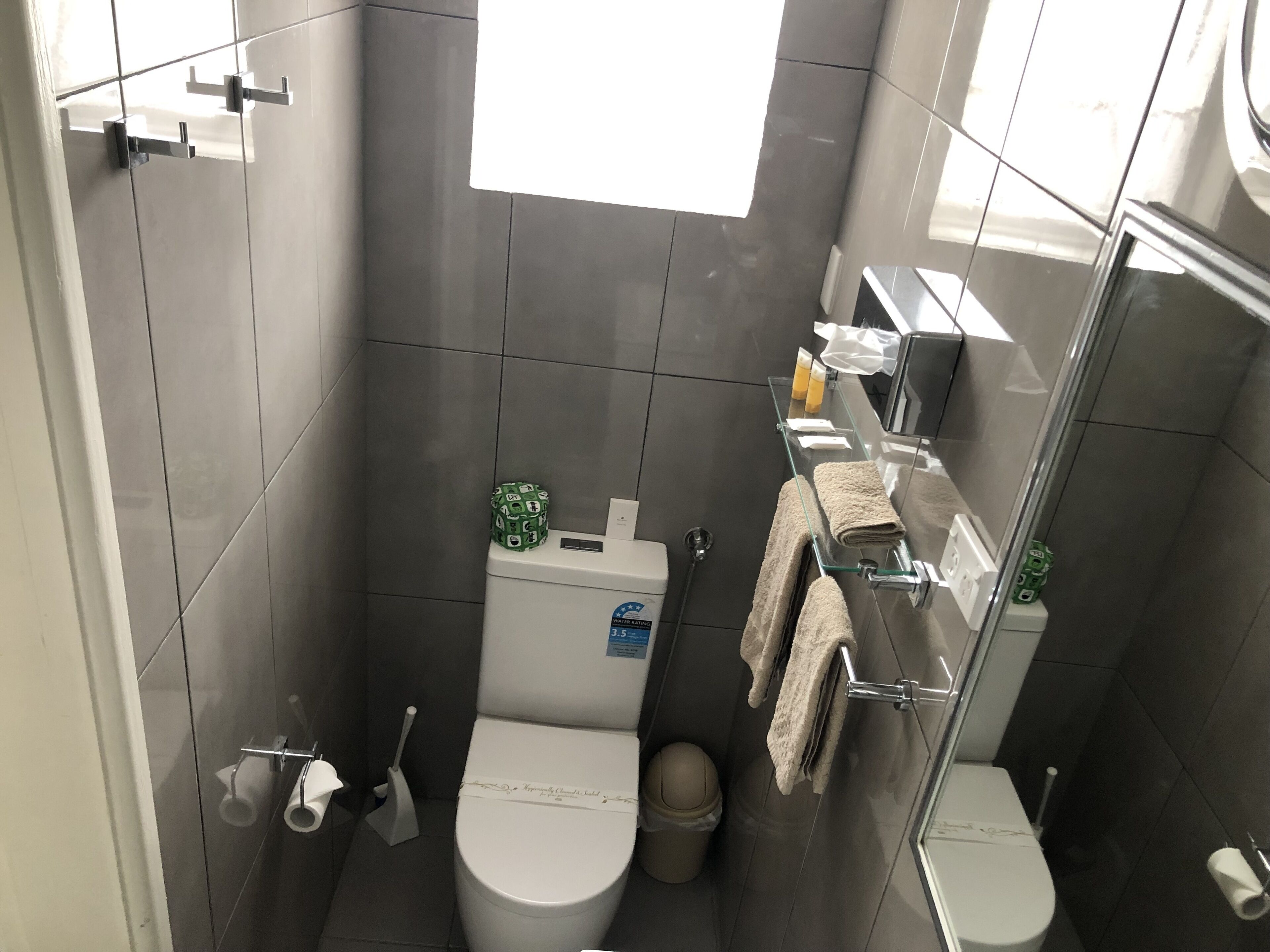 Casa de banho compacta com duas sanitas, cabine de duche em vidro e toucador pequeno com espelho.