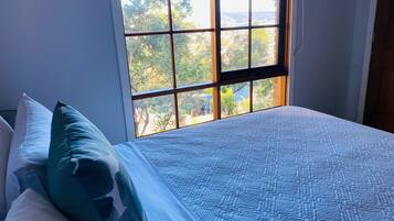 Quarto com uma janela grande, uma cama com colcha estampada e duas almofadas.