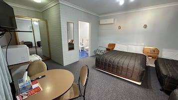 Quarto de hotel com cama, escrivaninha, cadeira, mesinha e espelho.