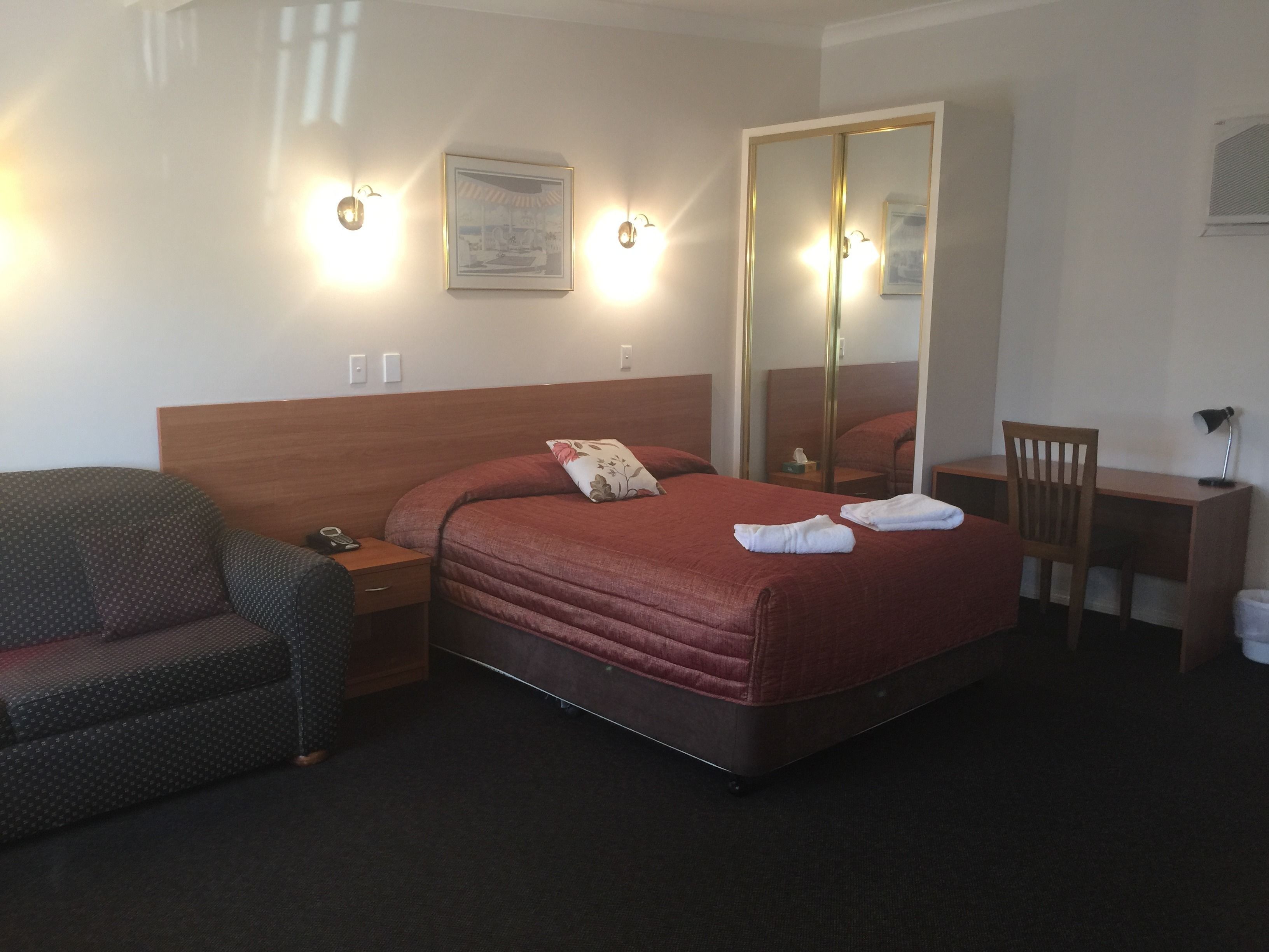 Quarto de hotel com cama, cadeira, escrivaninha e espelho.