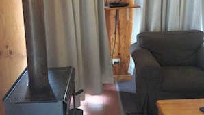Um quarto acolhedor com lareira a lenha, uma televisão sobre um suporte de madeira, um sofá e cortinas.