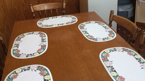 Uma mesa de jantar de madeira com jogos americanos florais e cadeiras.