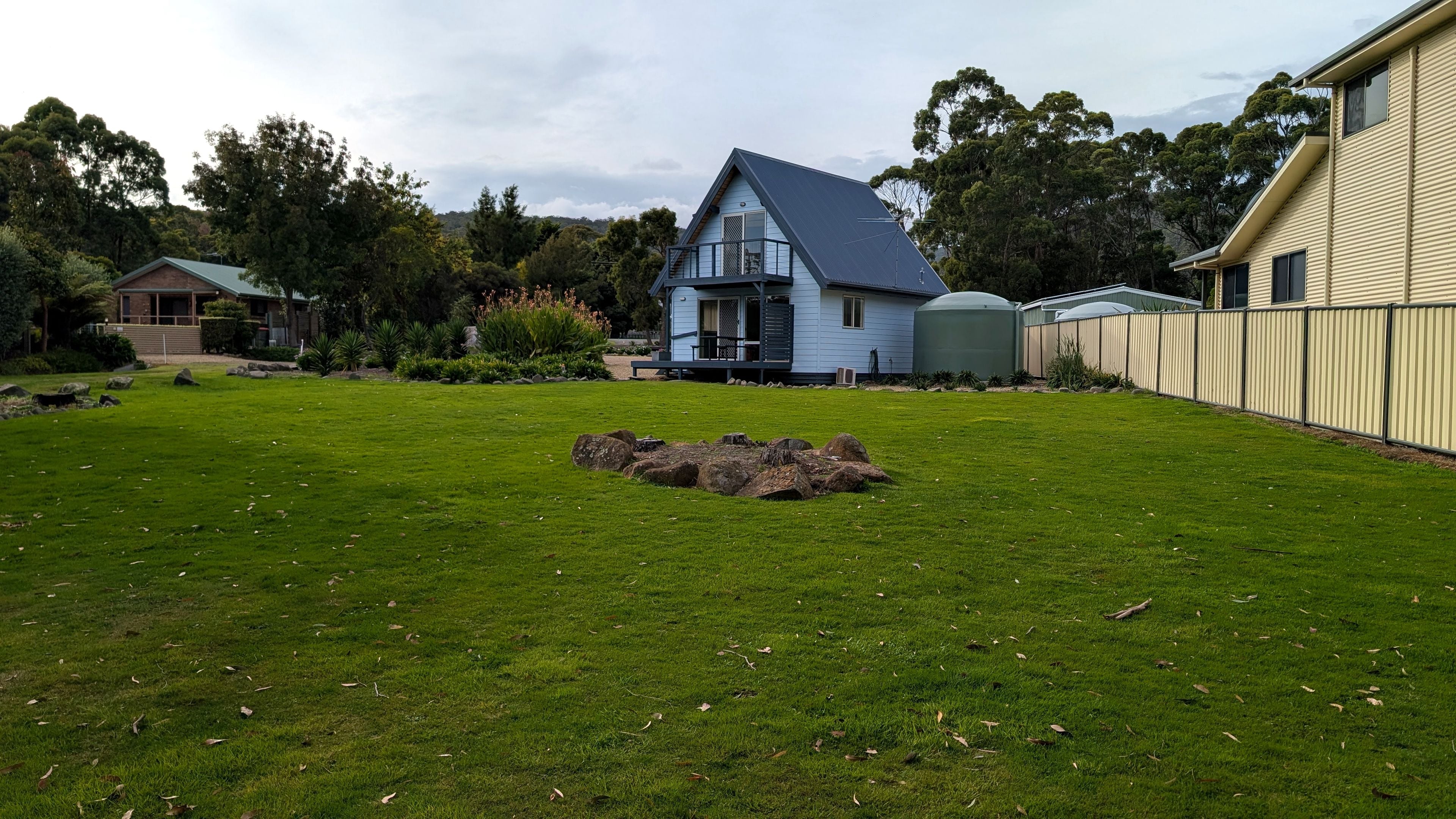 Um imóvel residencial com gramado bem cuidado, uma grande formação rochosa e uma casa com telhado azul e varanda.