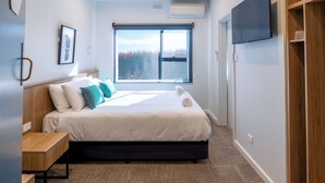 Quarto de hotel moderno com uma cama grande, uma escrivaninha, uma TV e uma janela com vista para a água.
