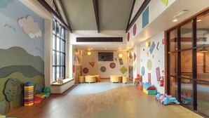 Uma sala de brincar infantil bem iluminada, com uma janela grande, piso de madeira e decorações coloridas nas paredes.