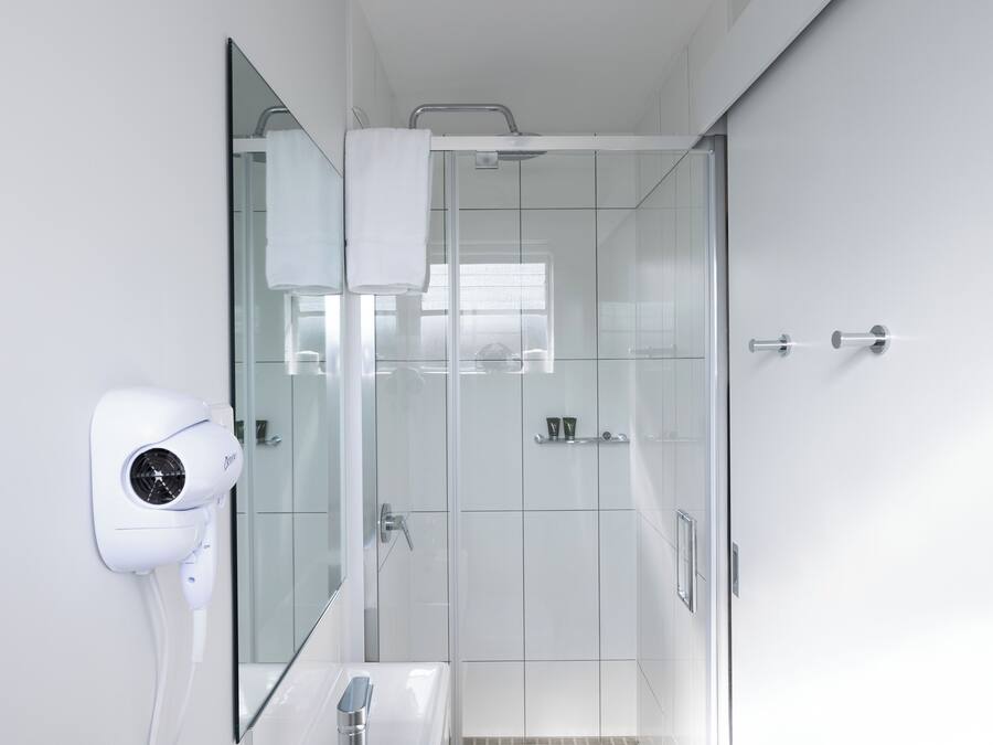 Uma casa de banho moderna com cabine de duche em vidro, uma toalha branca pendurada na porta e um secador de cabelo fixado na parede.