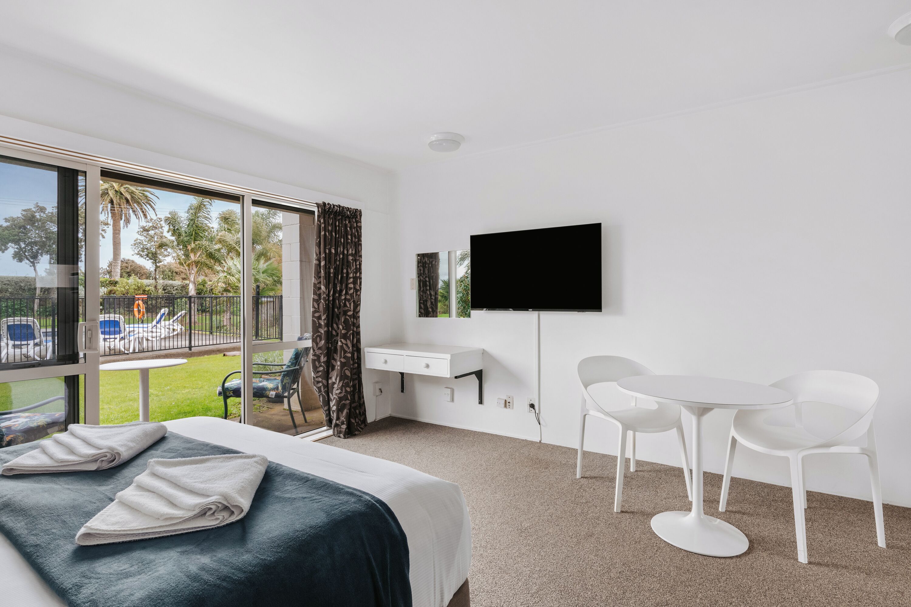 Quarto de hotel com cama, escrivaninha, televisão e vista para a área externa.