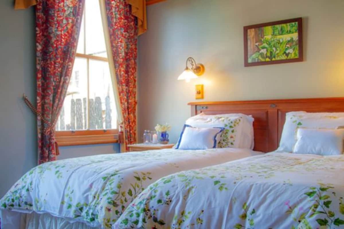 Uma cama de casal com roupa de cama florida, uma mesa de cabeceira com abajur e um quadro na parede.