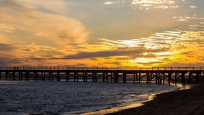 Um cais se estendendo para a água, com o pôr do sol ao fundo.