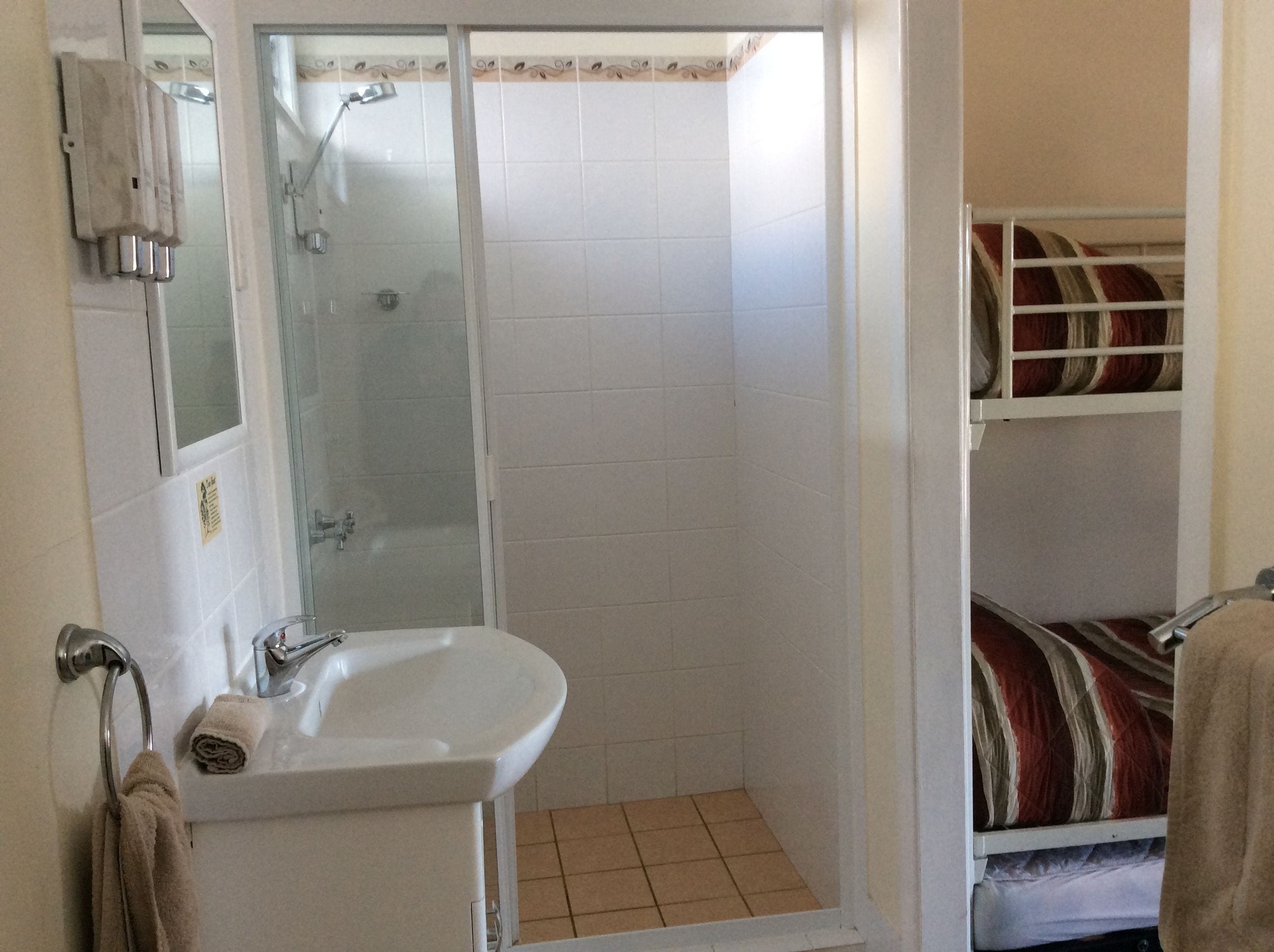 Casa de banho com cabine de duche em vidro, uma pia e uma cama com manta listrada.