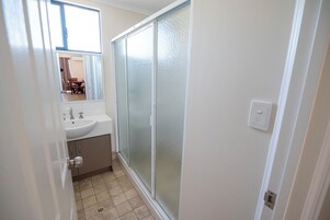 Casa de banho com uma pia branca, espelho e porta de chuveiro em vidro jateado.