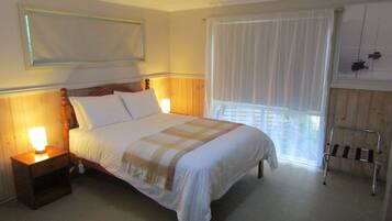 Cama bem arrumada com cabeceira de madeira, duas luminárias de apoio e uma janela com cortinas finas.