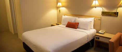 Quarto de hotel com uma cama grande, duas luminárias de cabeceira, uma mesa de cabeceira, uma cadeira e uma porta.
