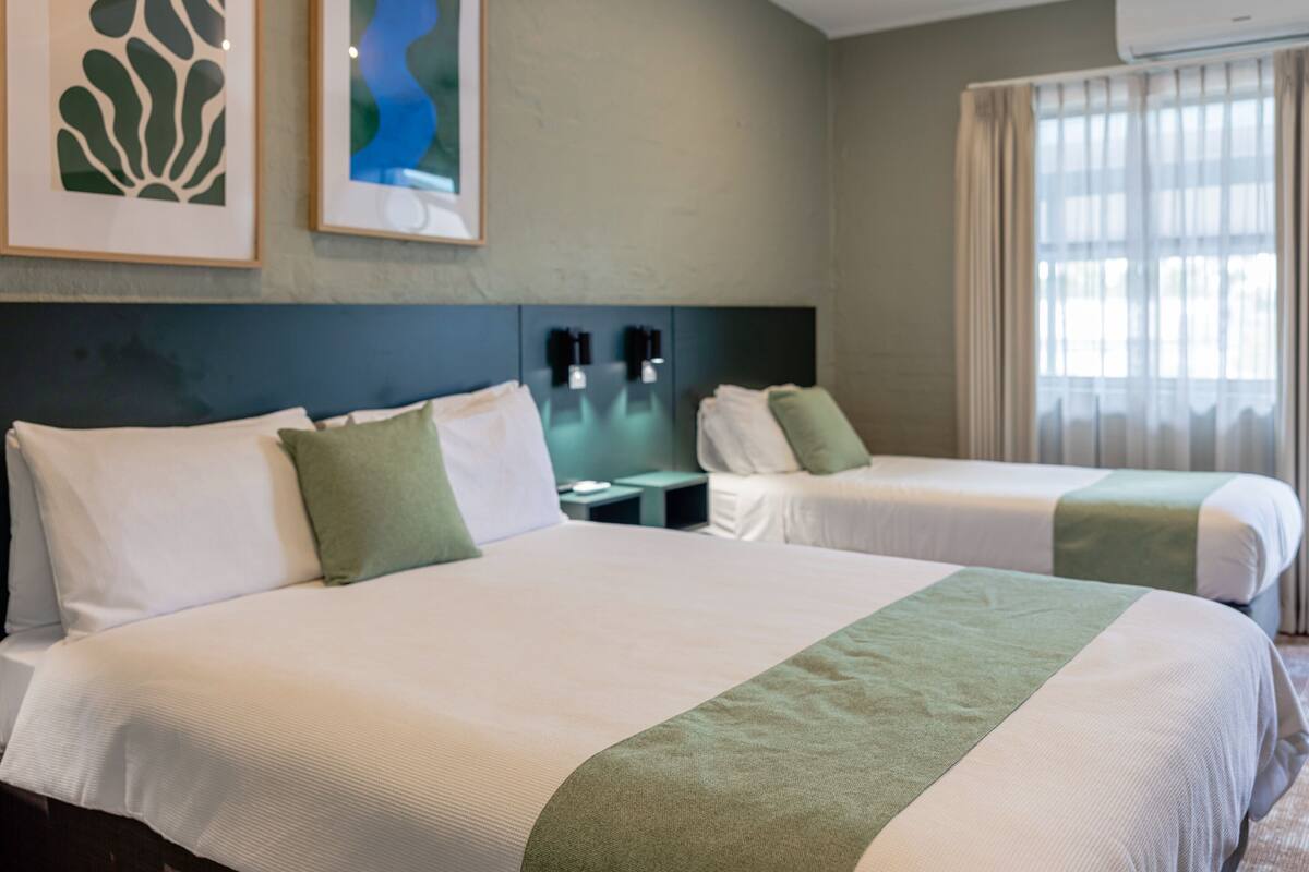 Quarto de hotel com duas camas, cabeceira, mesas de cabeceira e uma obra de arte na parede.