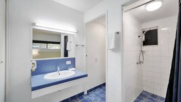 Casa de banho com lavatório branco, bancada azul e chuveiro com azulejos brancos.