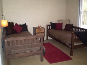 Quarto pequeno e acolhedor com cama de madeira, mesa de cabeceira, abajur e tapete vermelho.