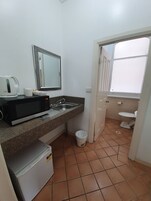 Casa de banho compacta com lavatório, espelho e sanita. É visível um micro-ondas e um frigorífico pequeno.