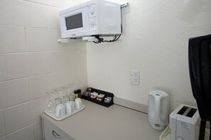 Uma cozinha compacta com micro-ondas, torradeira e um tabuleiro com copos e acompanhamentos.